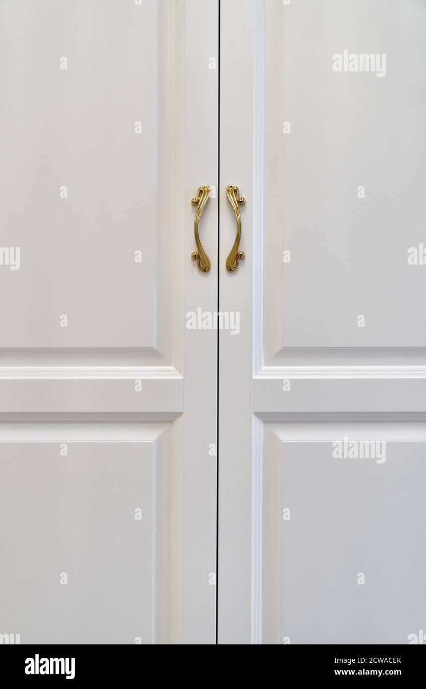Classic white wardrobe with with ornamental golden handles close-up ...