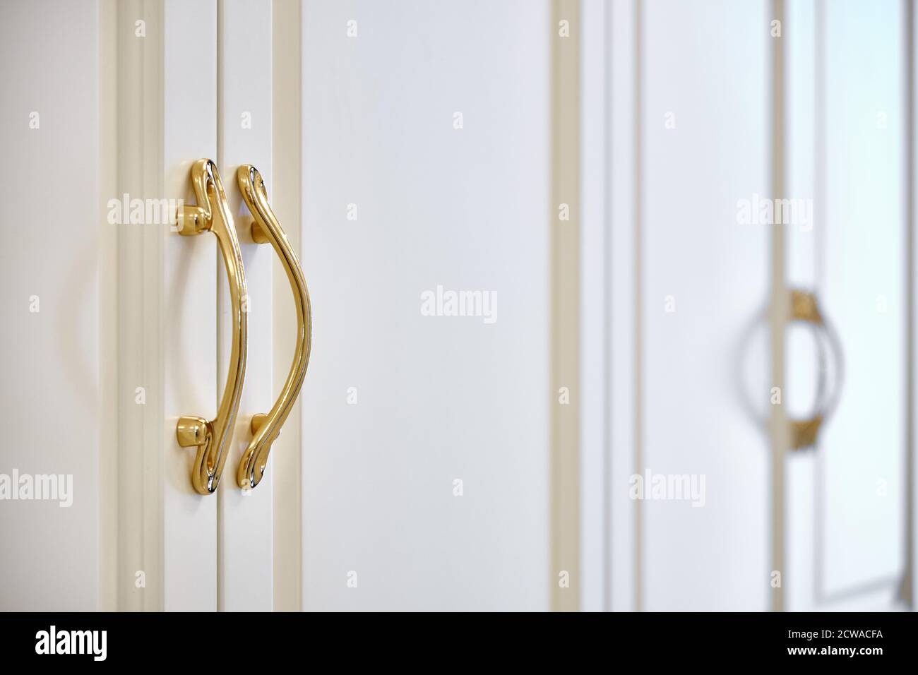 Classic white wardrobe with with ornamental golden handles close-up ...