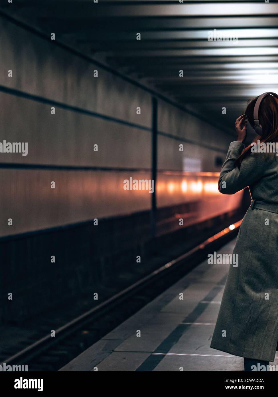 Selective focus. Back view of a girl in a gray coat with headphones on ...