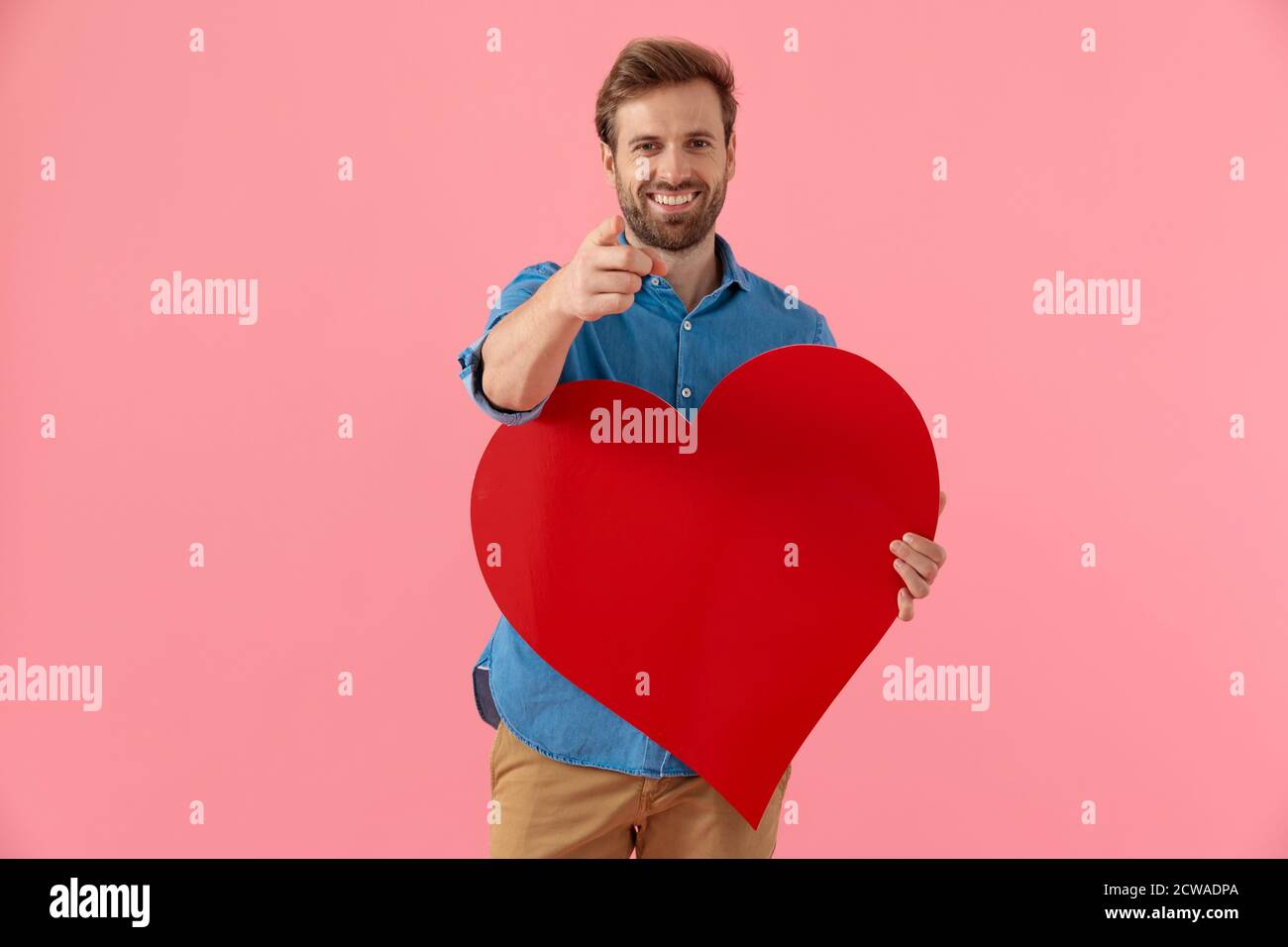 happy casual guy smiling and holding big red heart, pointing finger and ...