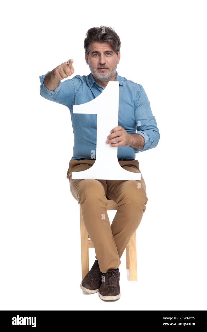 Confident casual man holding a number one and pointing forward while ...