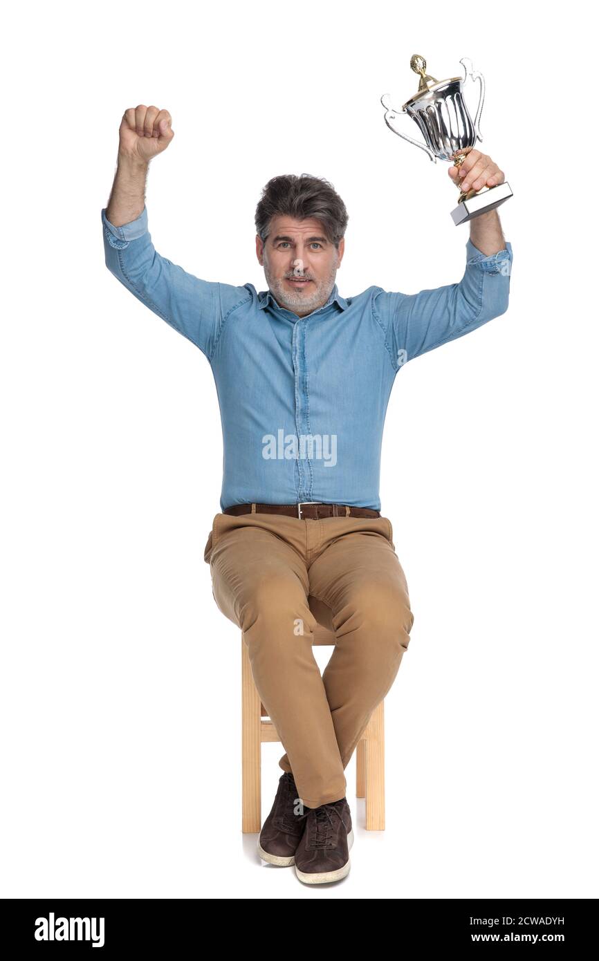 Cheerful casual man holding a trophy and celebrating with his hands in ...