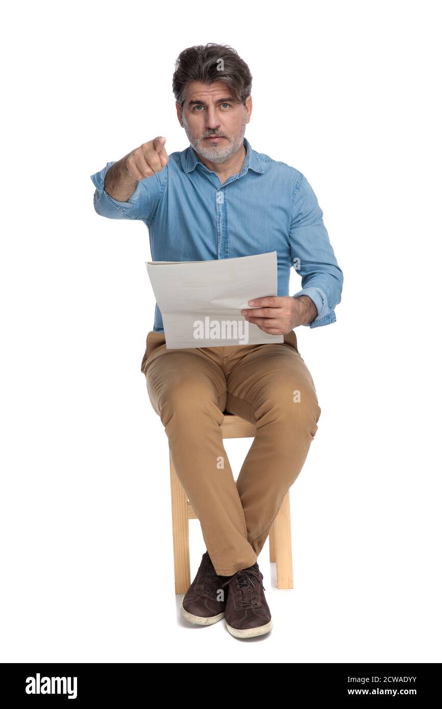 Confident casual man holding a newspaper and pointing forward while ...