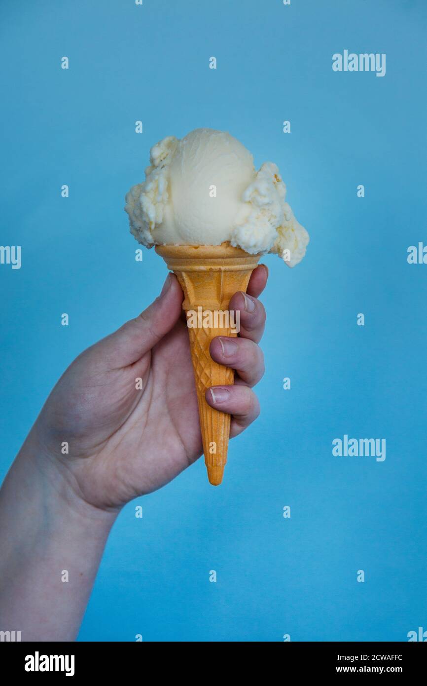 Hand holding a scoop of ice cream in a cone with blue background Stock ...