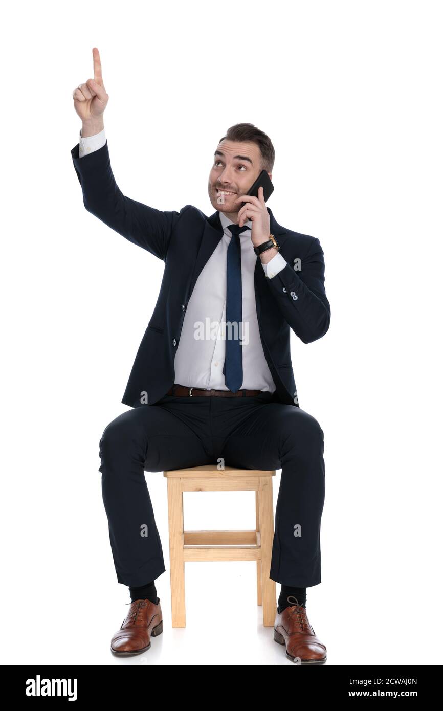 Positive businessman talking on phone and pointing up, smiling while ...