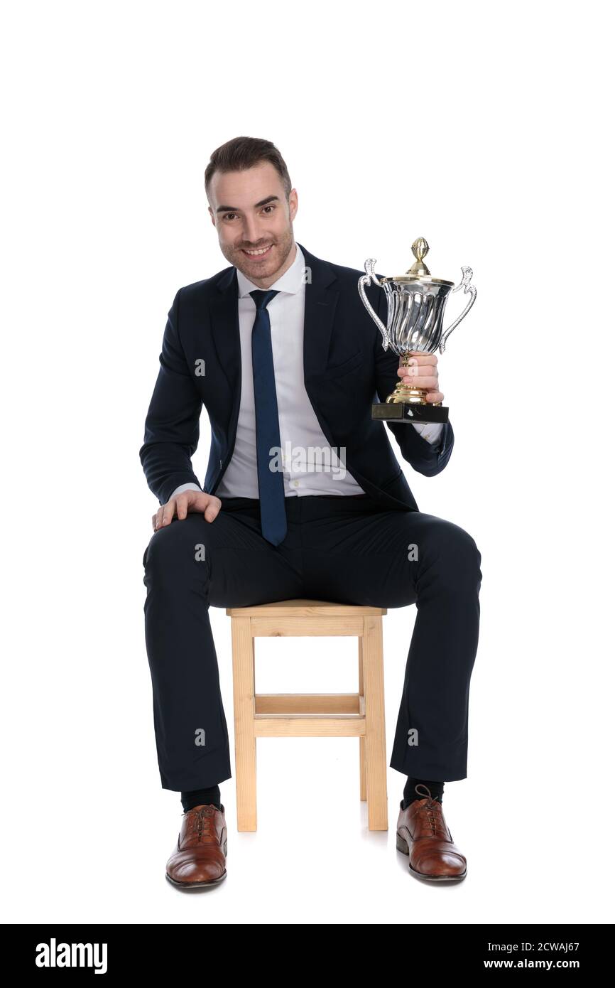Happy businessman smiling and holding trophy while sitting on a chair ...