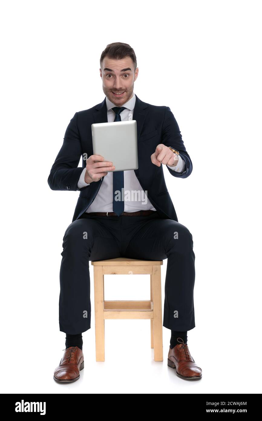 Positive businessman pointing forward, smiling and holding tablet while ...