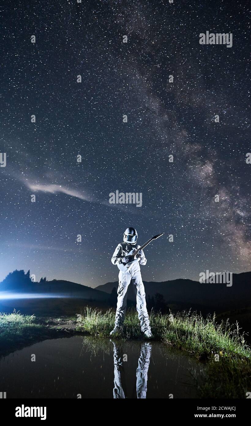 Spaceman in space suit and helmet playing guitar under blue night sky ...