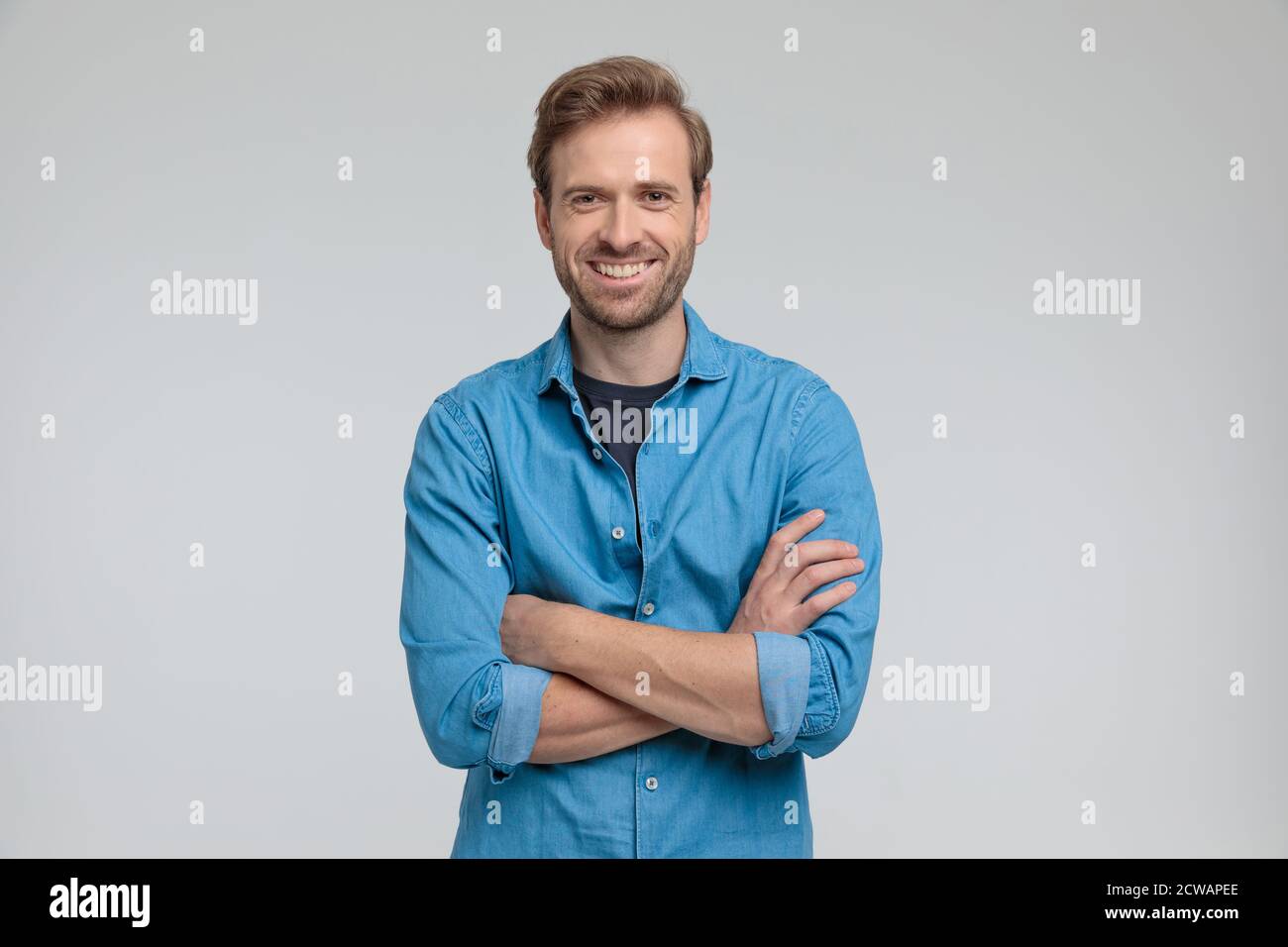 enthusiastic young casual man crossing arms and smiling on grey ...