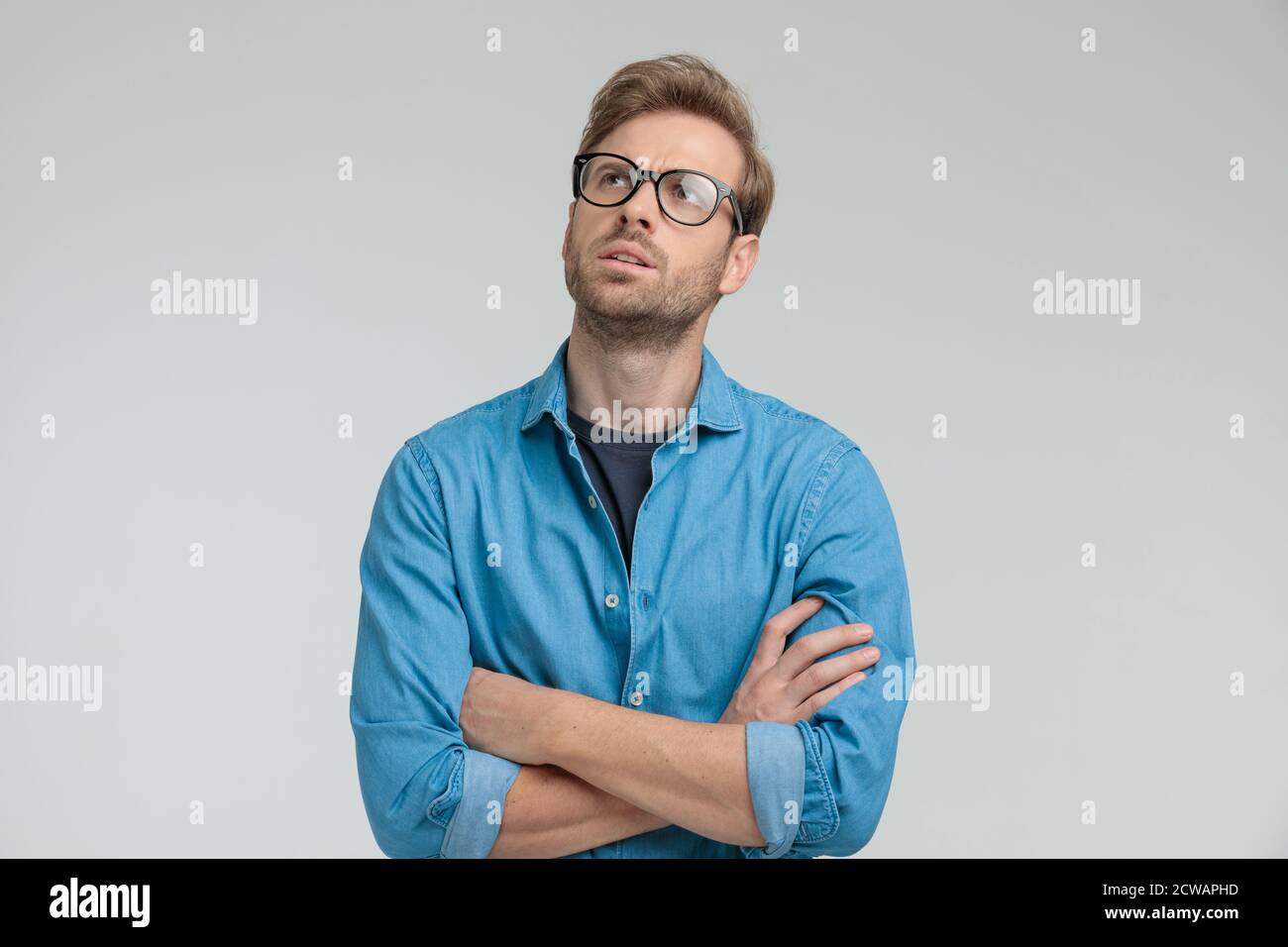 confused young casual man looking up and thinking, crossing arms on ...