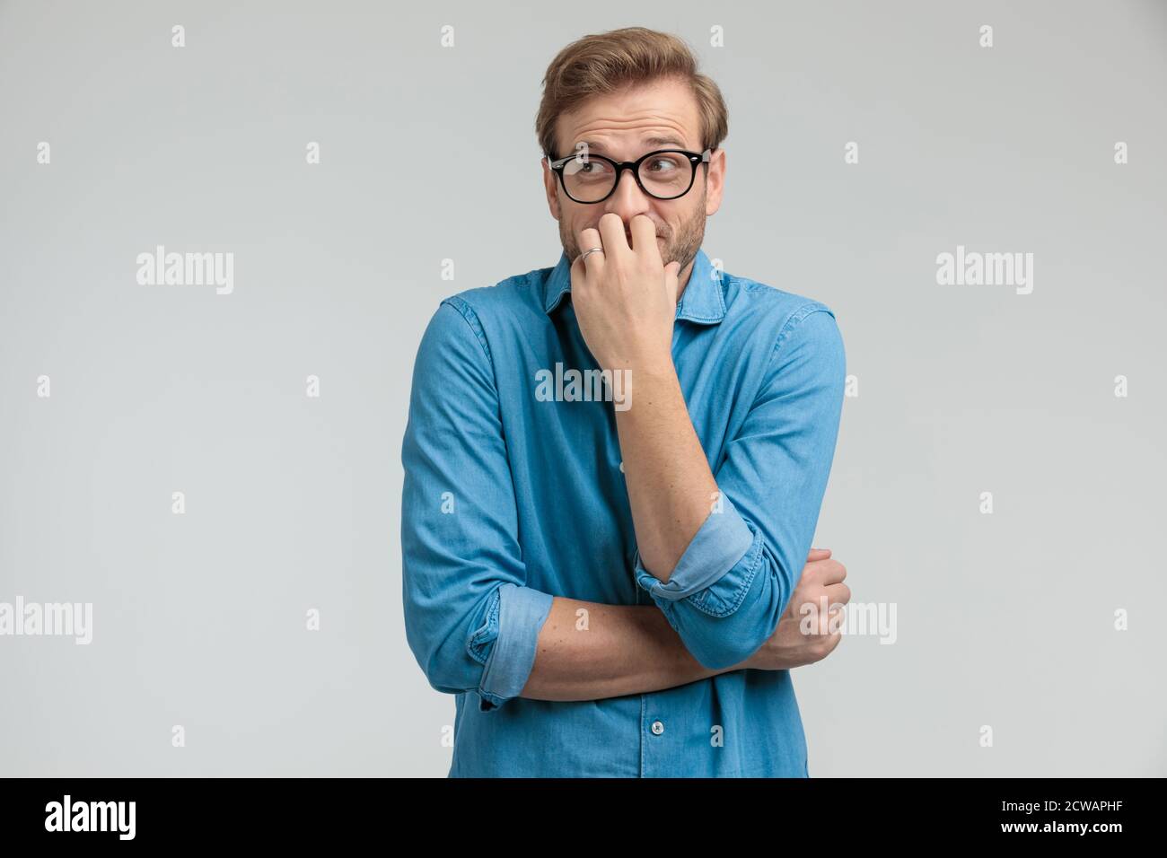 thoughtful young casual man holding hand to mouth and waiting on grey ...