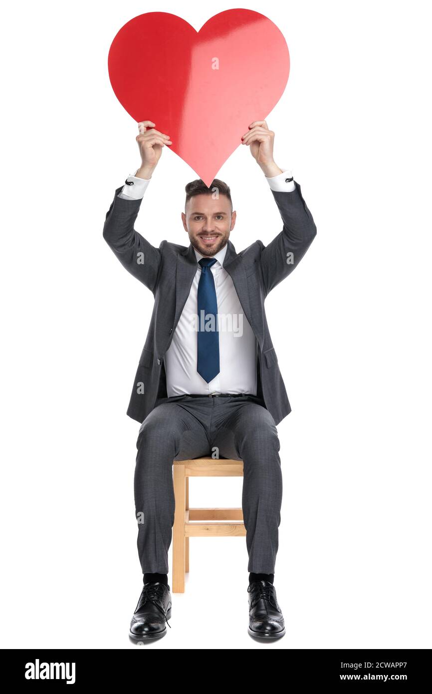 happy young man holding big red heart above head and smiling, sitting ...