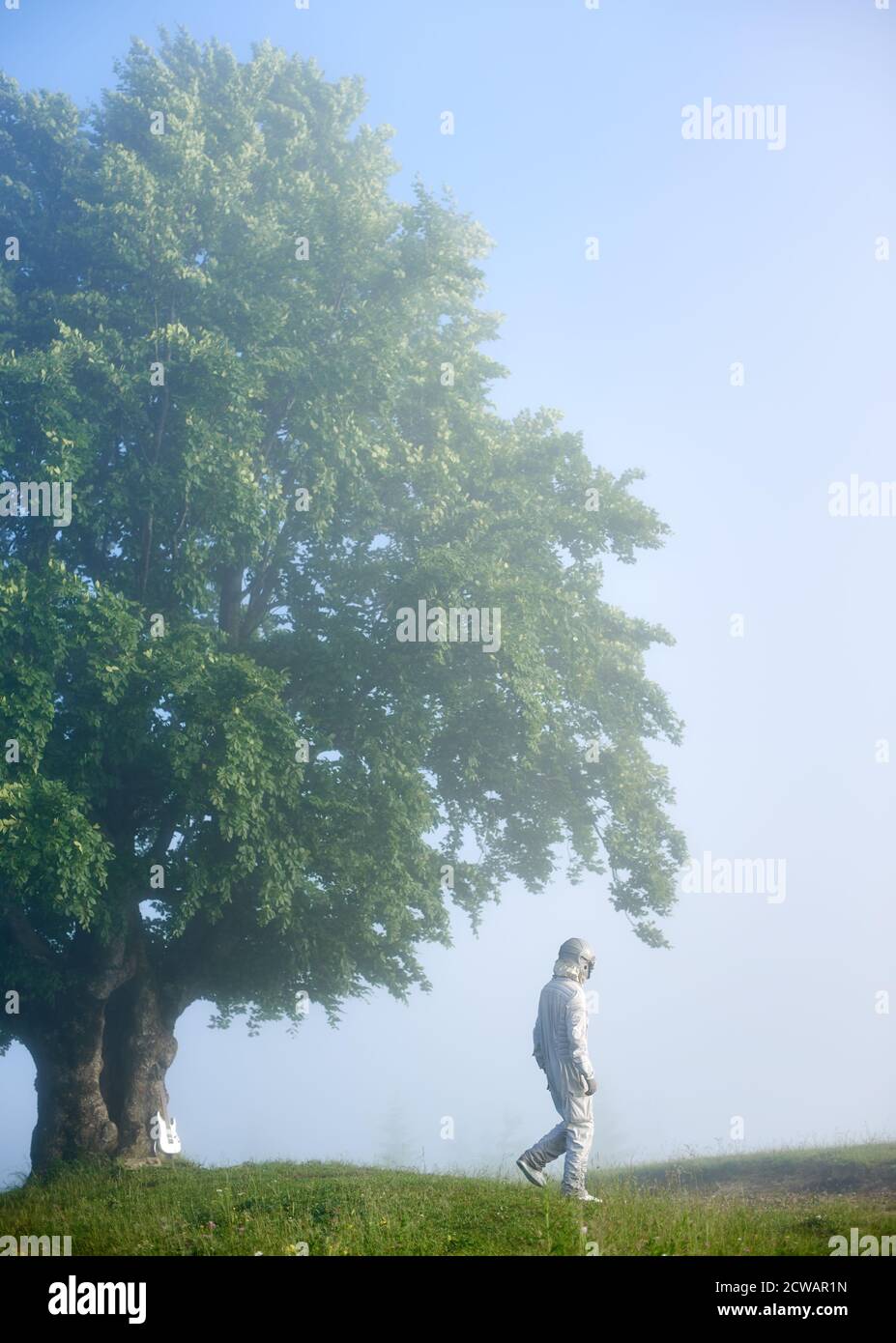 Back view of spaceman in space suit walking away from tree in foggy ...