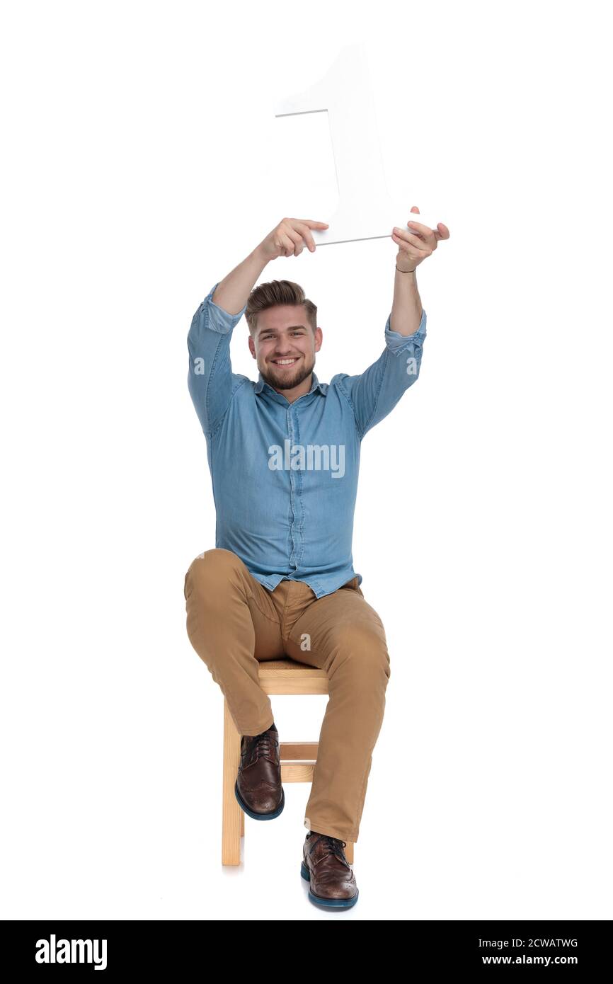 casual young man smiling and holding up number one sign, sitting ...
