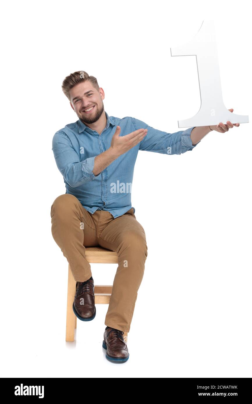 smiling casual man presenting number one sign to side, sitting isolated ...