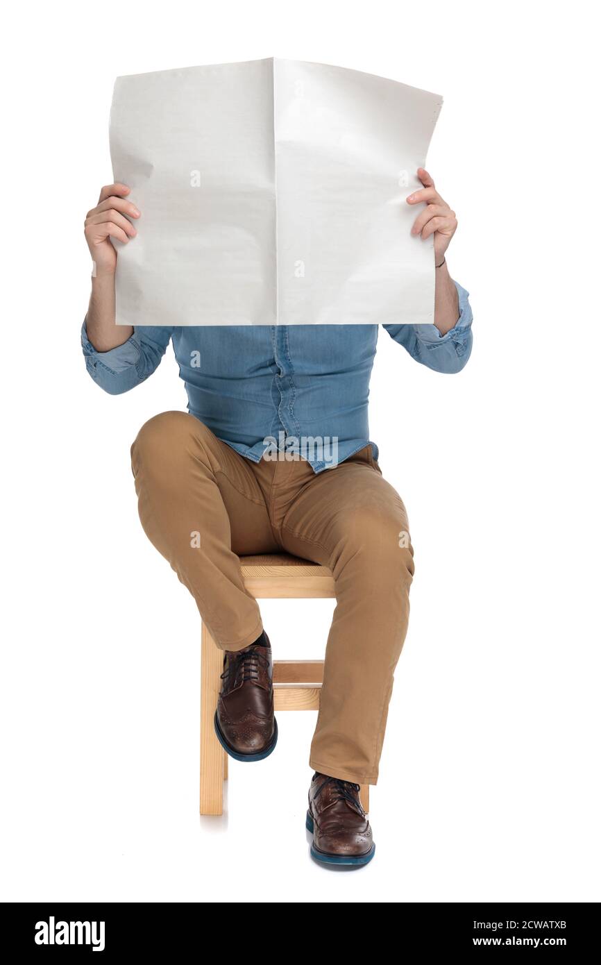 casual young man in denim shirt hiding behind newspaper, sitting ...