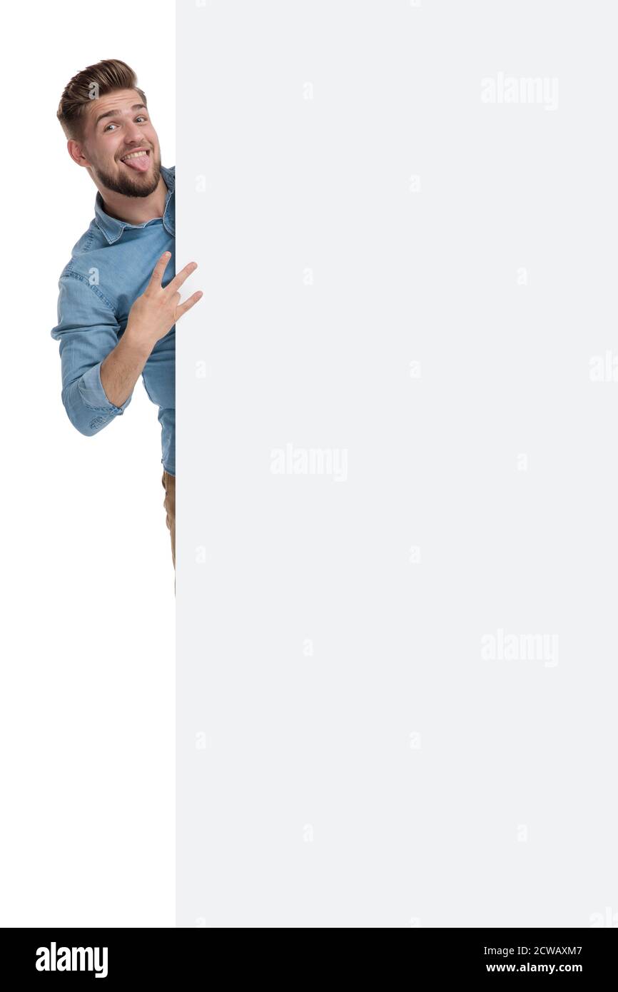Casual man making a funny face and sign behind a blank billboard while ...