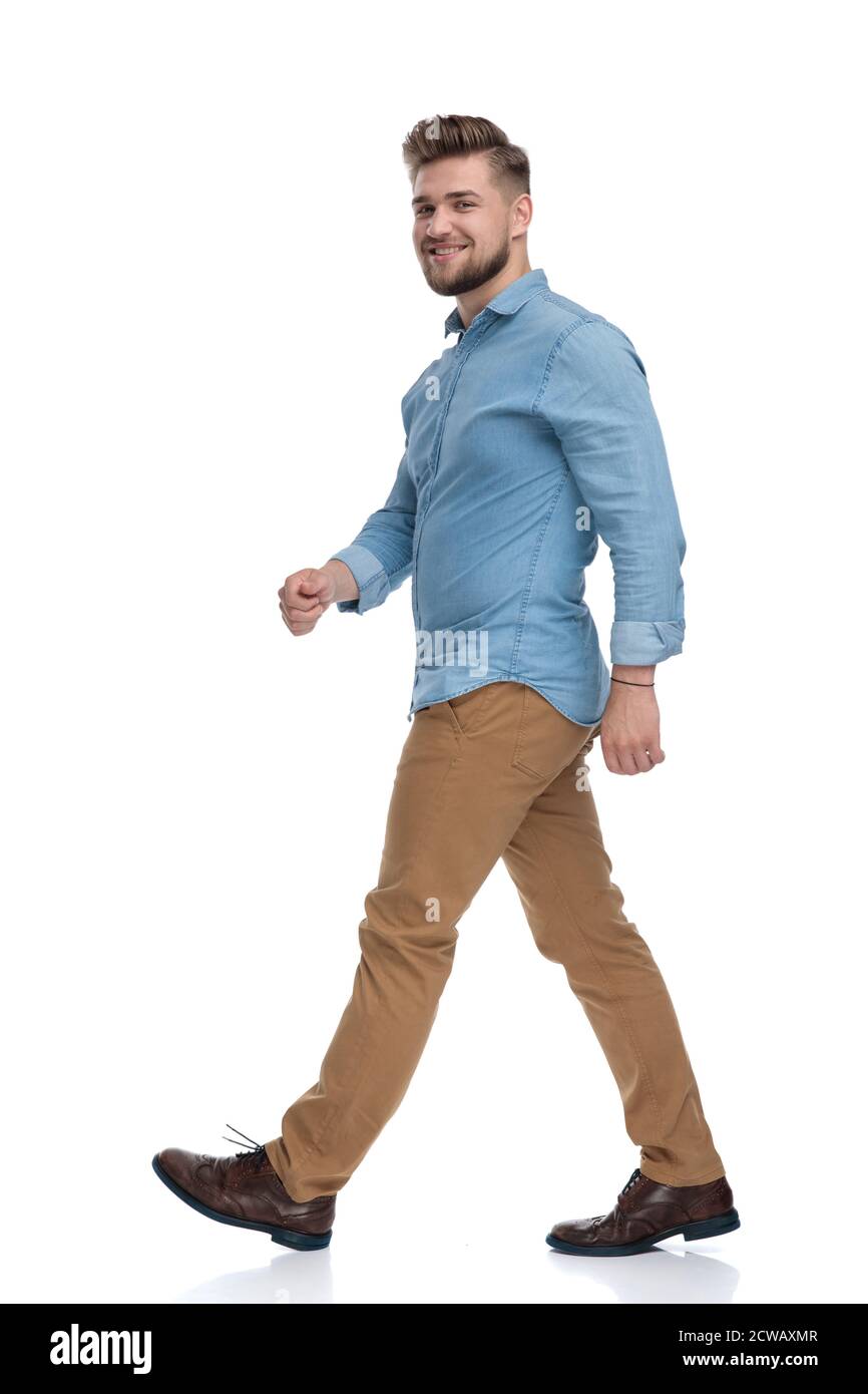 Side view of a confident casual man walking on white studio background ...
