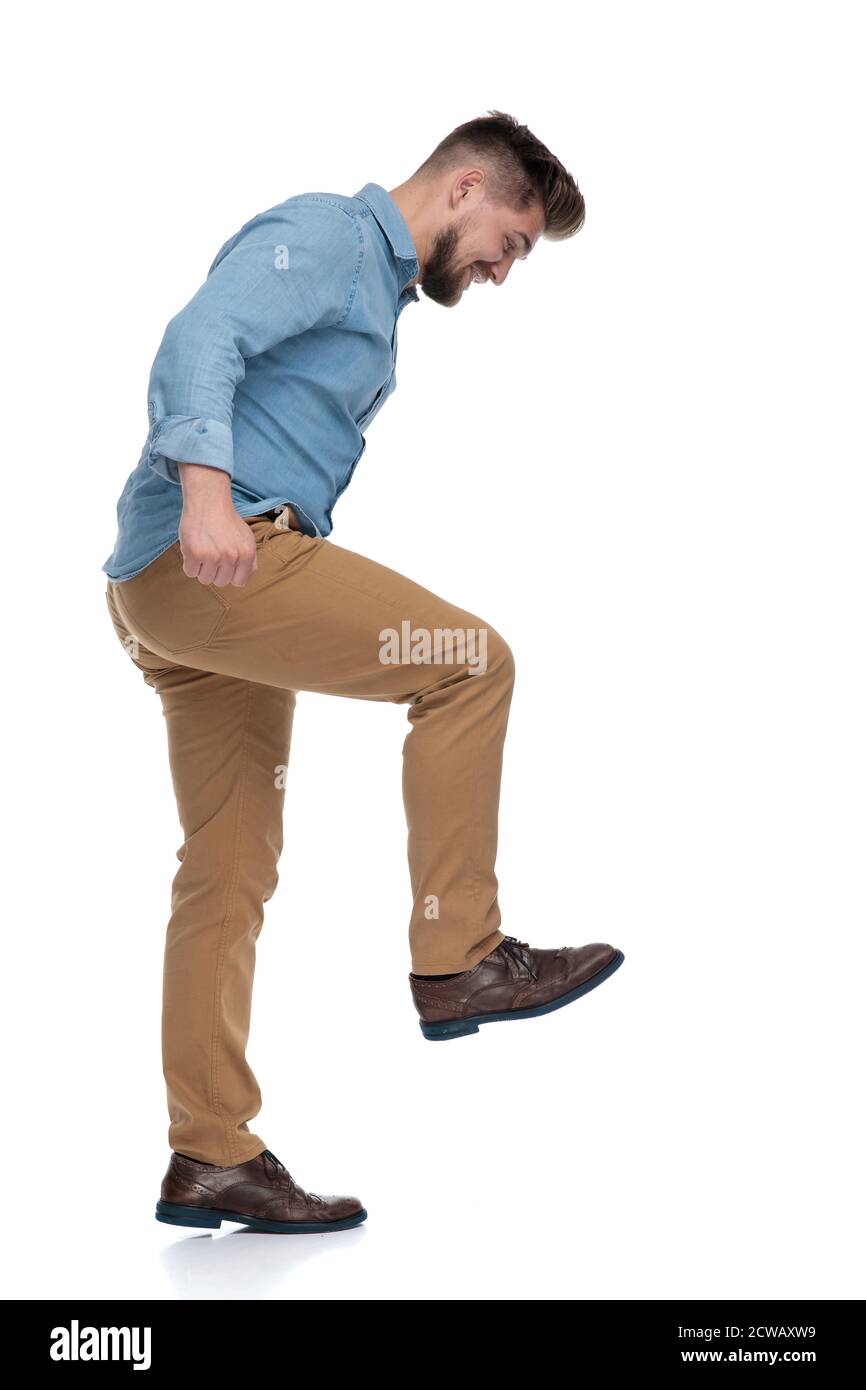 Side view of a young casual man stepping and laughing on white studio ...