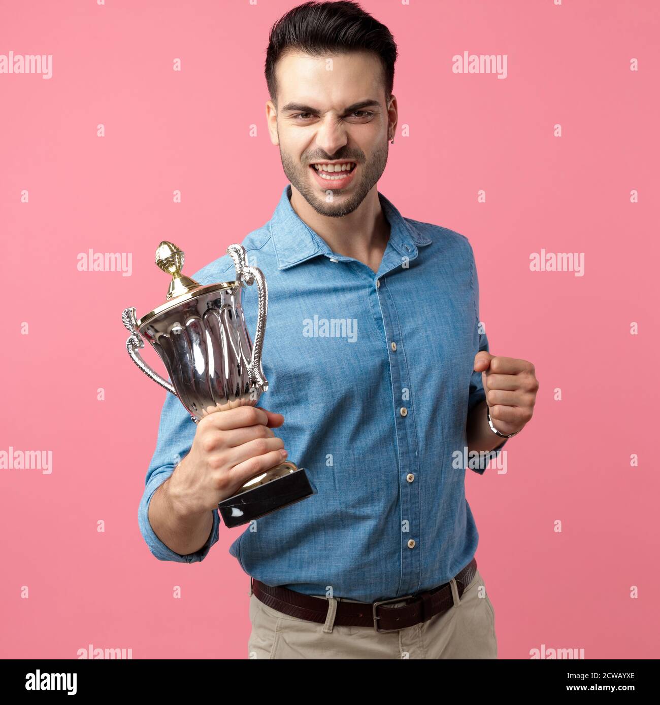 casual young man holding trophy and celebrating victory on pink ...