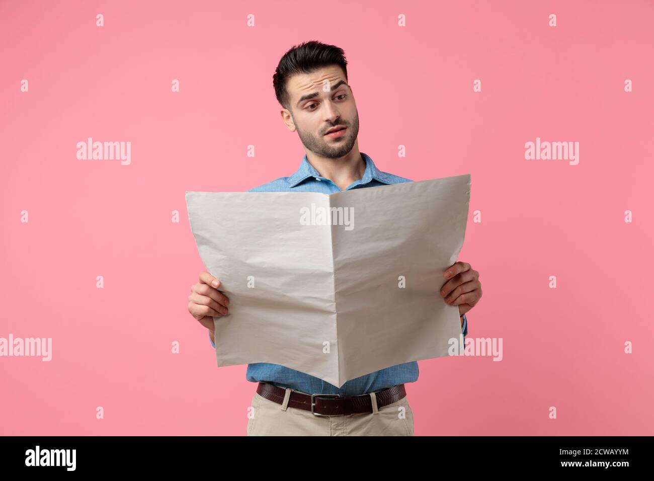 surprised young casual man reading newspaper, standing on pink ...