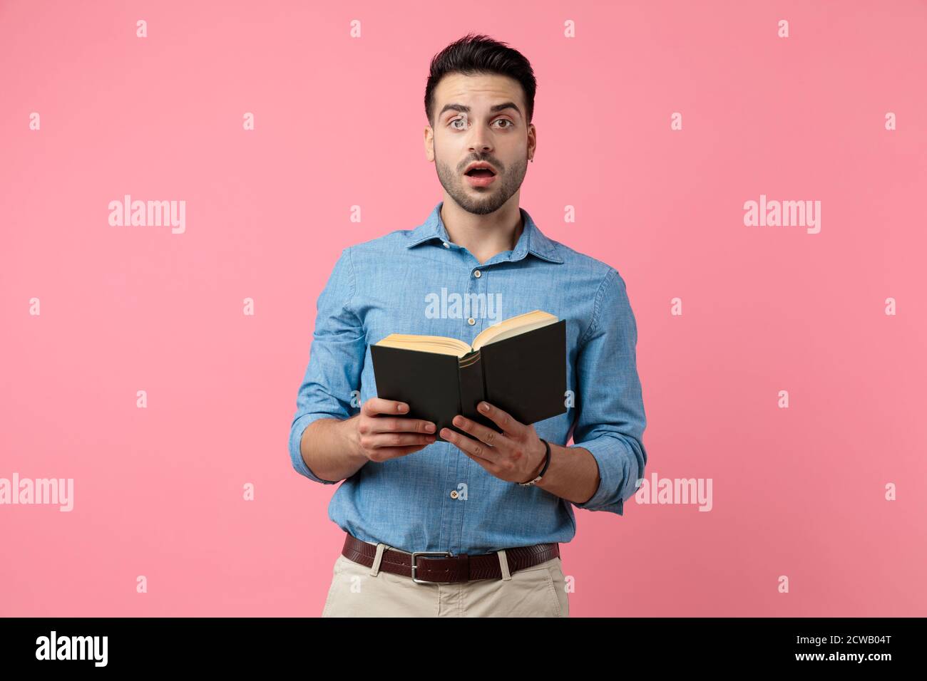 shocked young casual guy reading book and standing on pink background ...