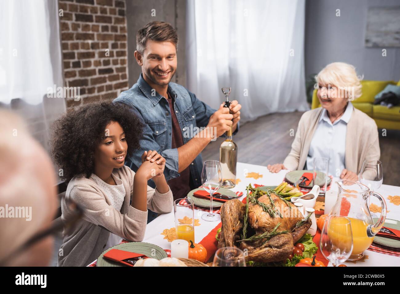 selective focus of man opening bottle of white wine during thanksgiving ...