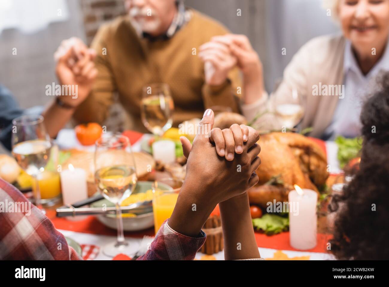 cropped view of multicultural family holding hands while praying during ...