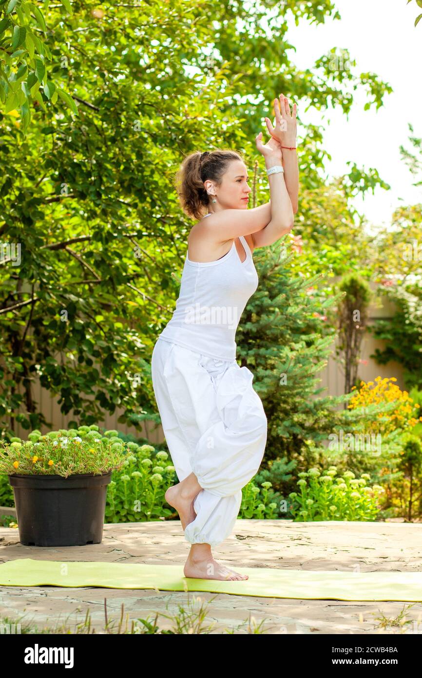 Young woman practices yoga in the summer garden - Garudasana or Eagle ...