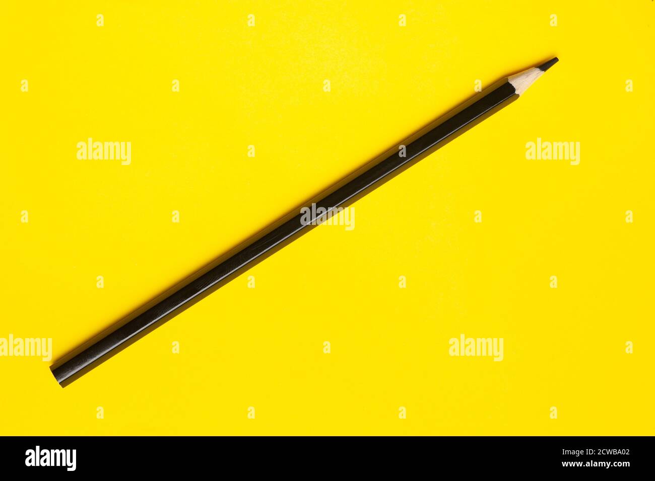 diagonal black sharp wooden pencil on a bright yellow background ...