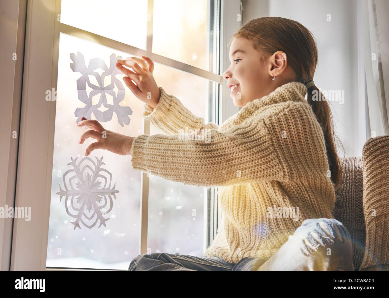 Cute little girl sitting by the window and looking at the winter forest ...