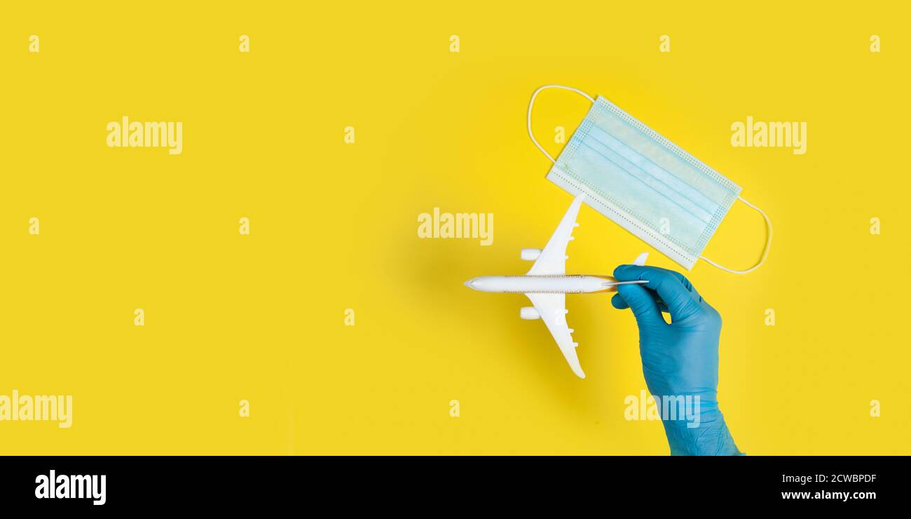 Hand in glove holding model airplane over face mask. Air travel resumes ...