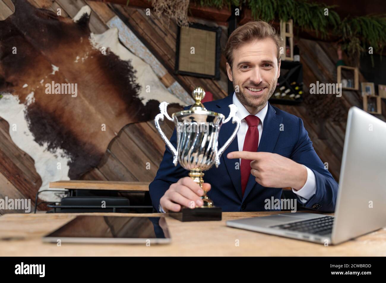 proud businessman pointing finger to trophy and smiling, sitting in a ...