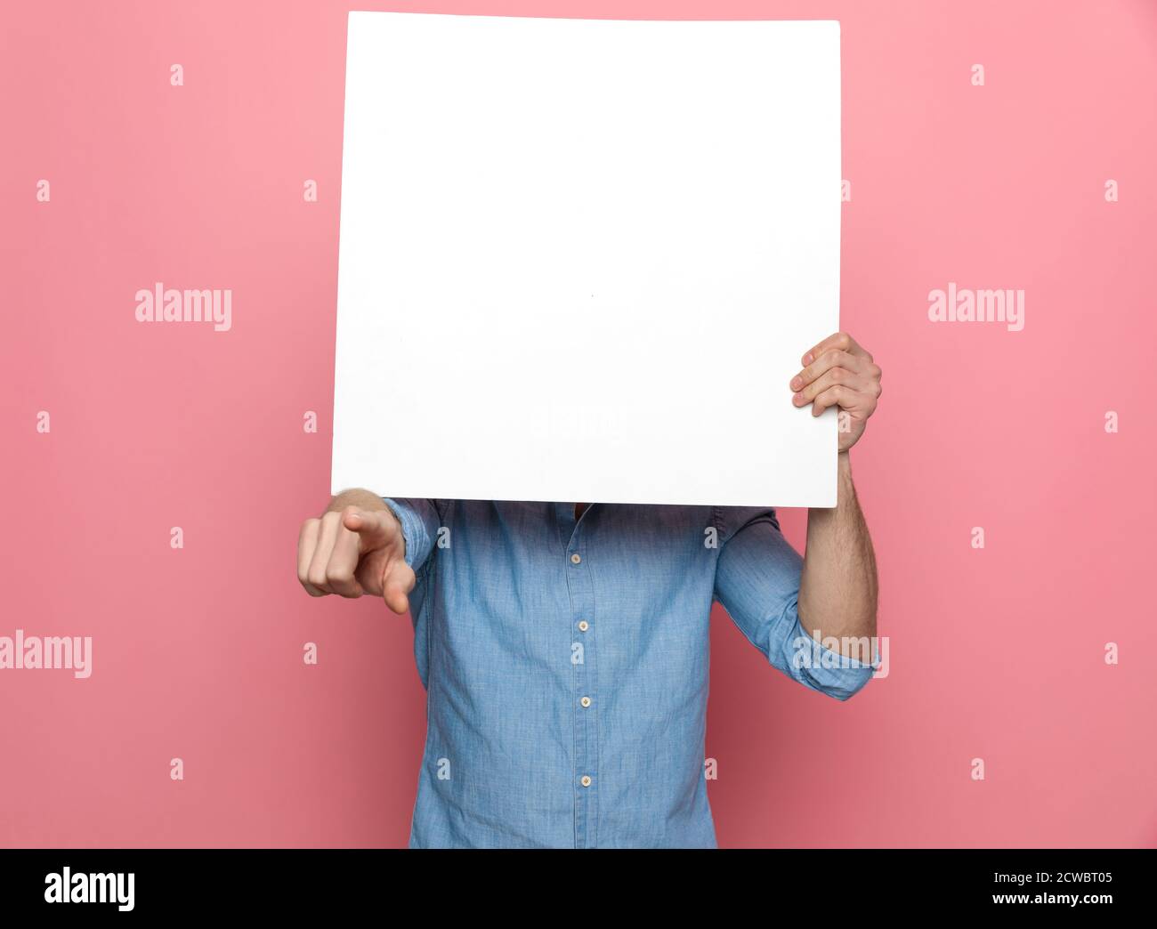 casual young guy in denim shirt hiding behind empty board and pointing ...