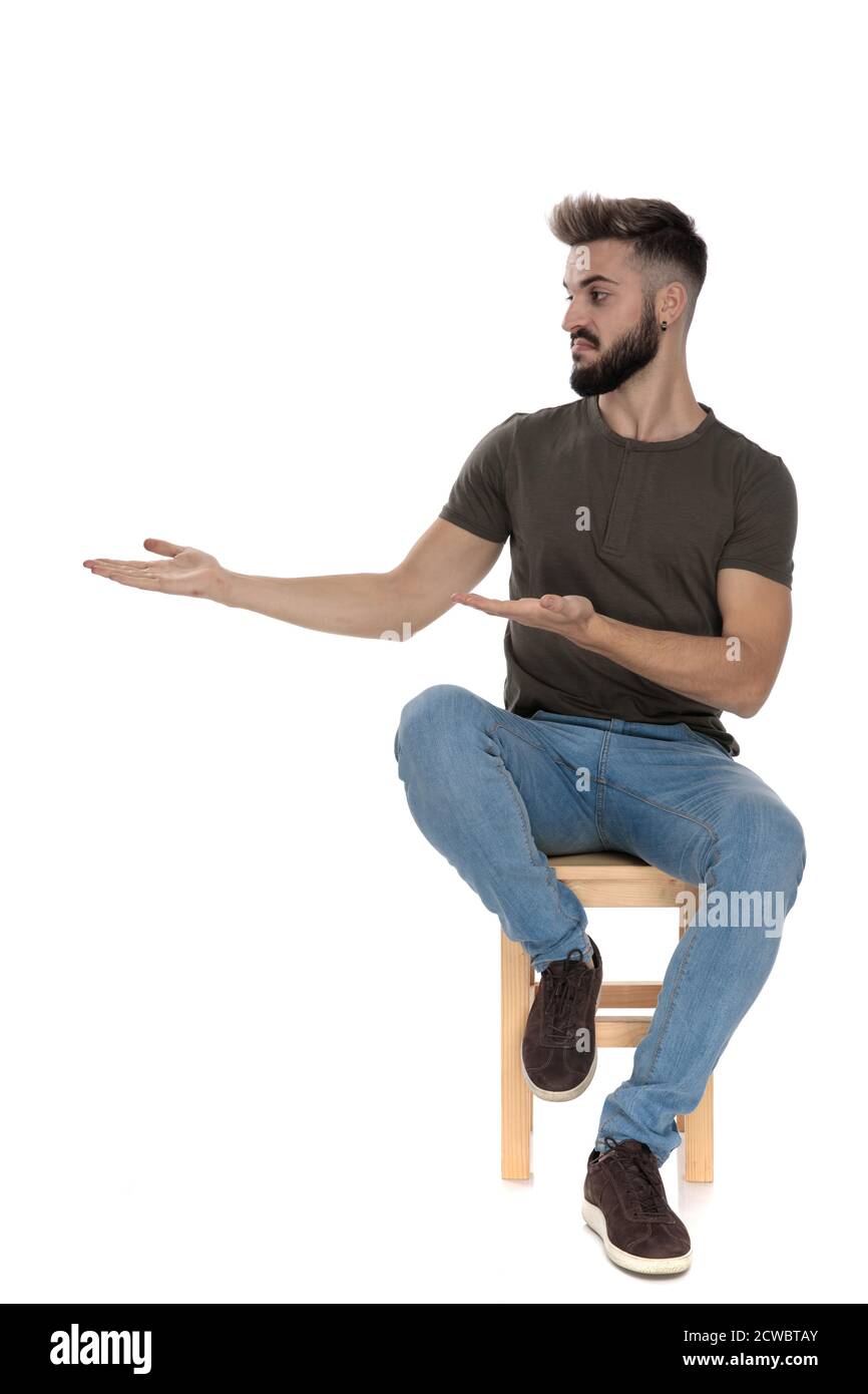 Bothered casual man presenting and explaining while sitting on a chair ...