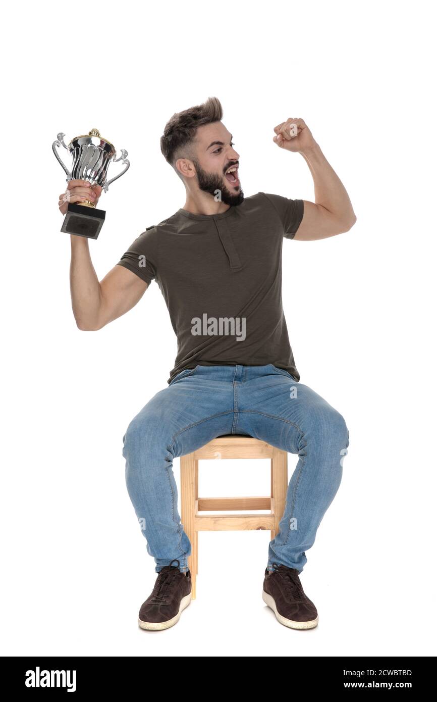 Winning casual man holding a trophy and shouting while sitting on a ...