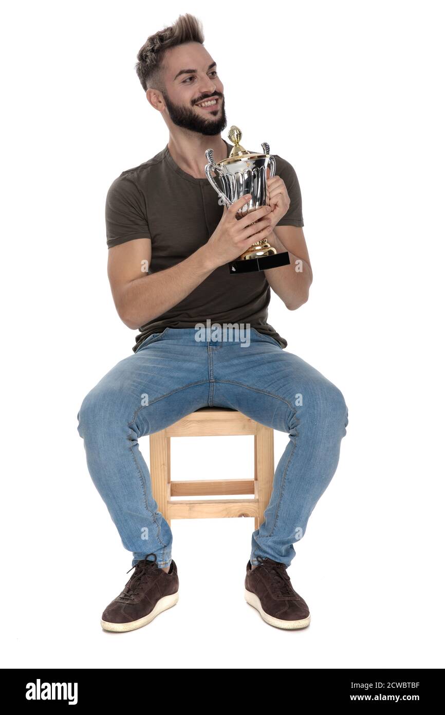 Cheerful casual man holding a trophy and smiling while sitting on a ...