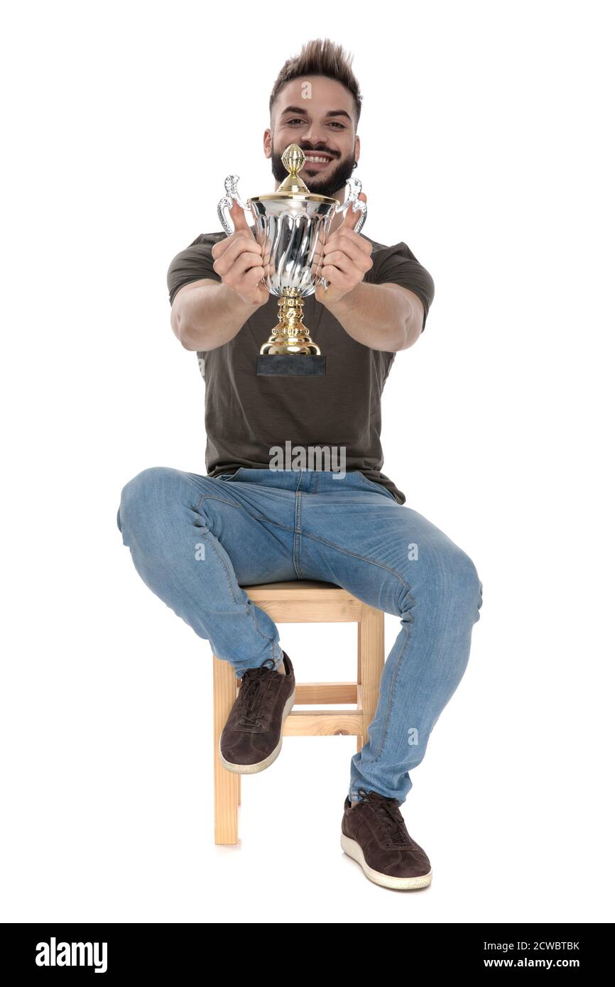 Proud casual man presenting his trophy and smiling while sitting on a ...