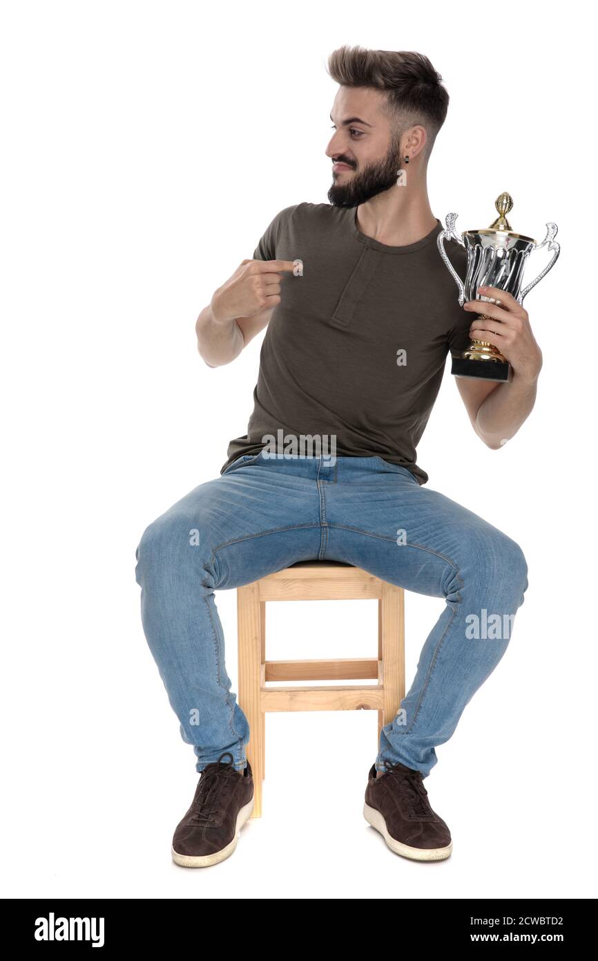 Happy casual man holding a trophy and pointing at it while sitting on a ...