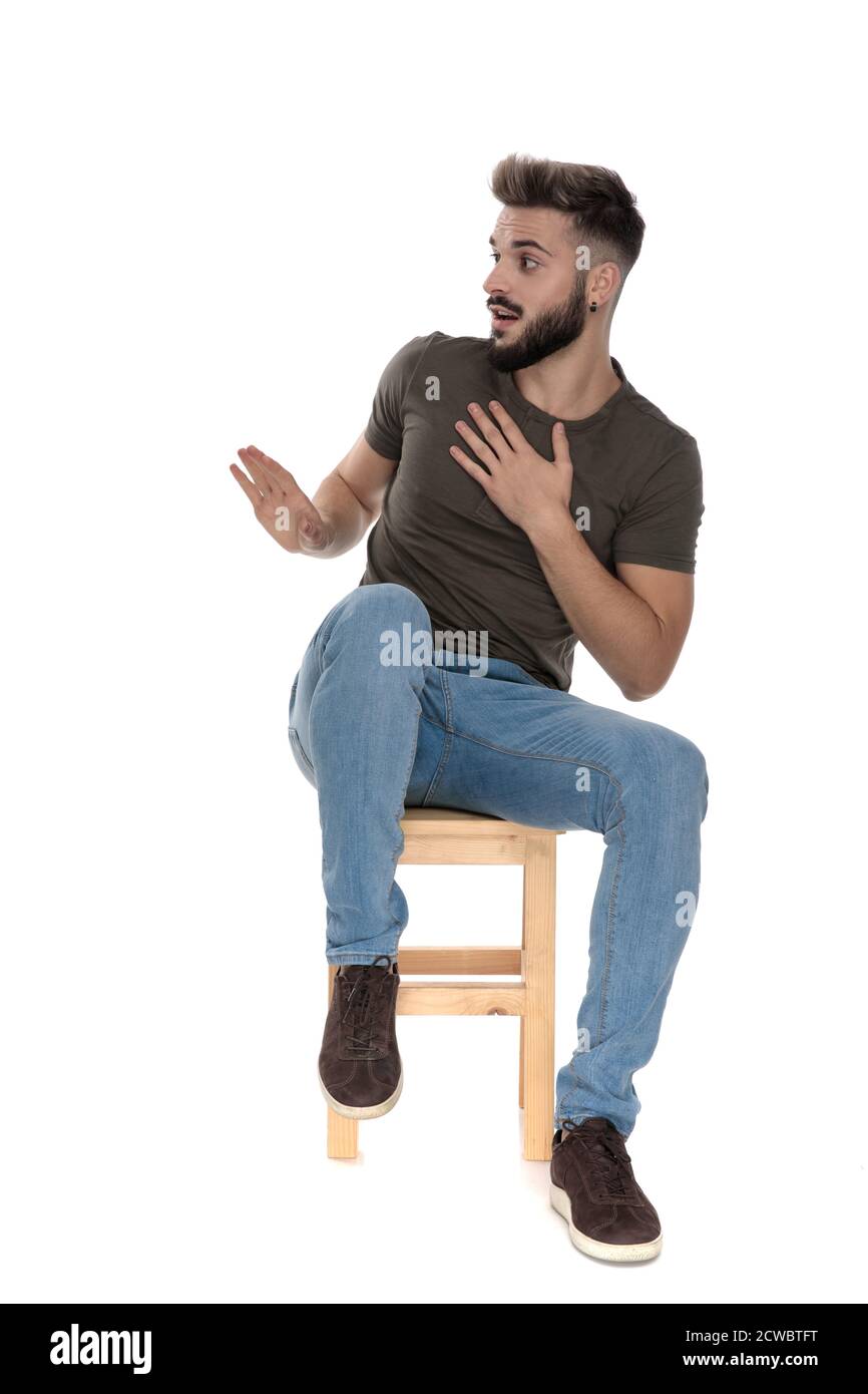 Surprised casual man apologizing while sitting on a chair on white ...
