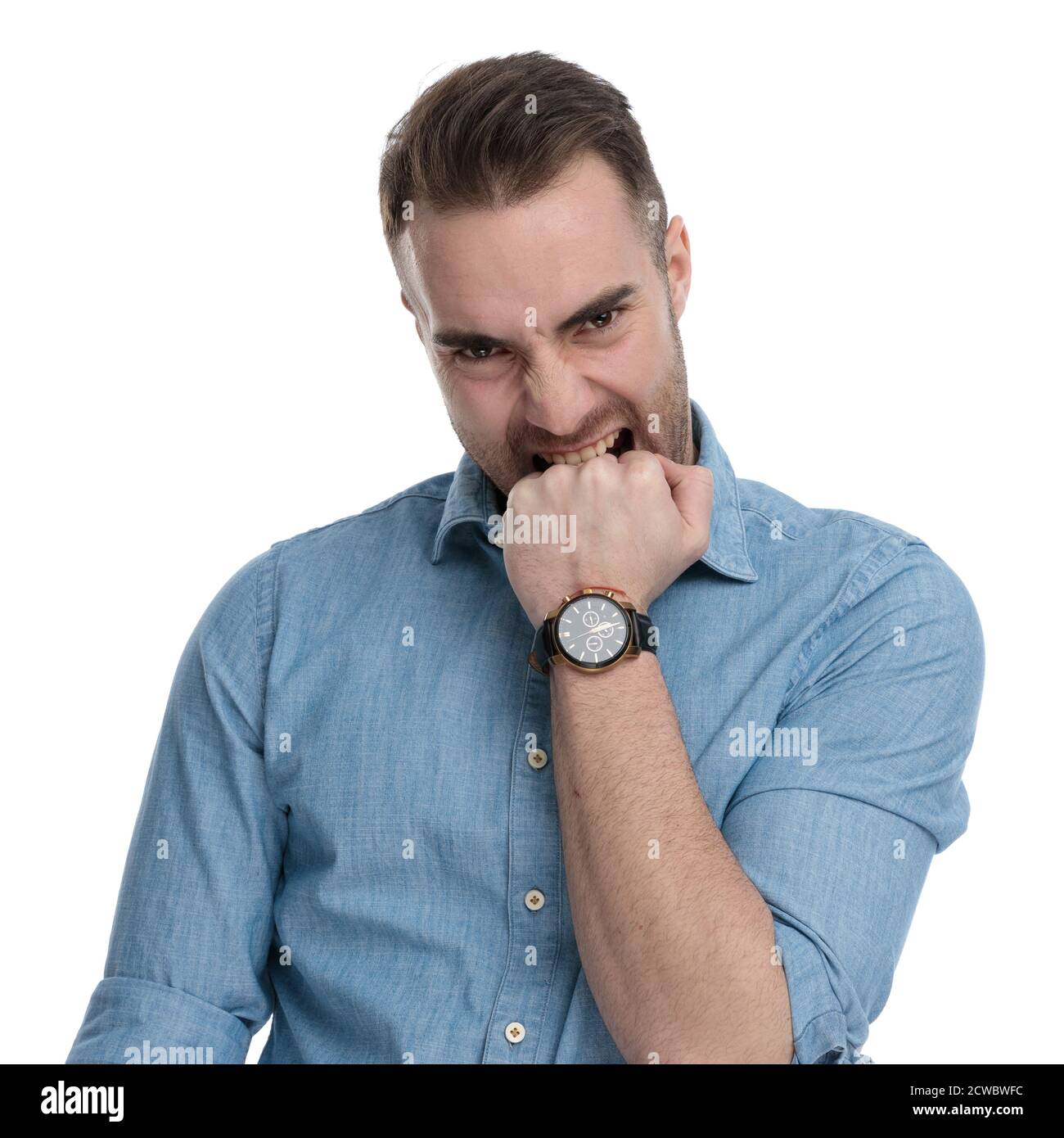 Angry casual man biting his fist while wearing blue shirt, standing on ...