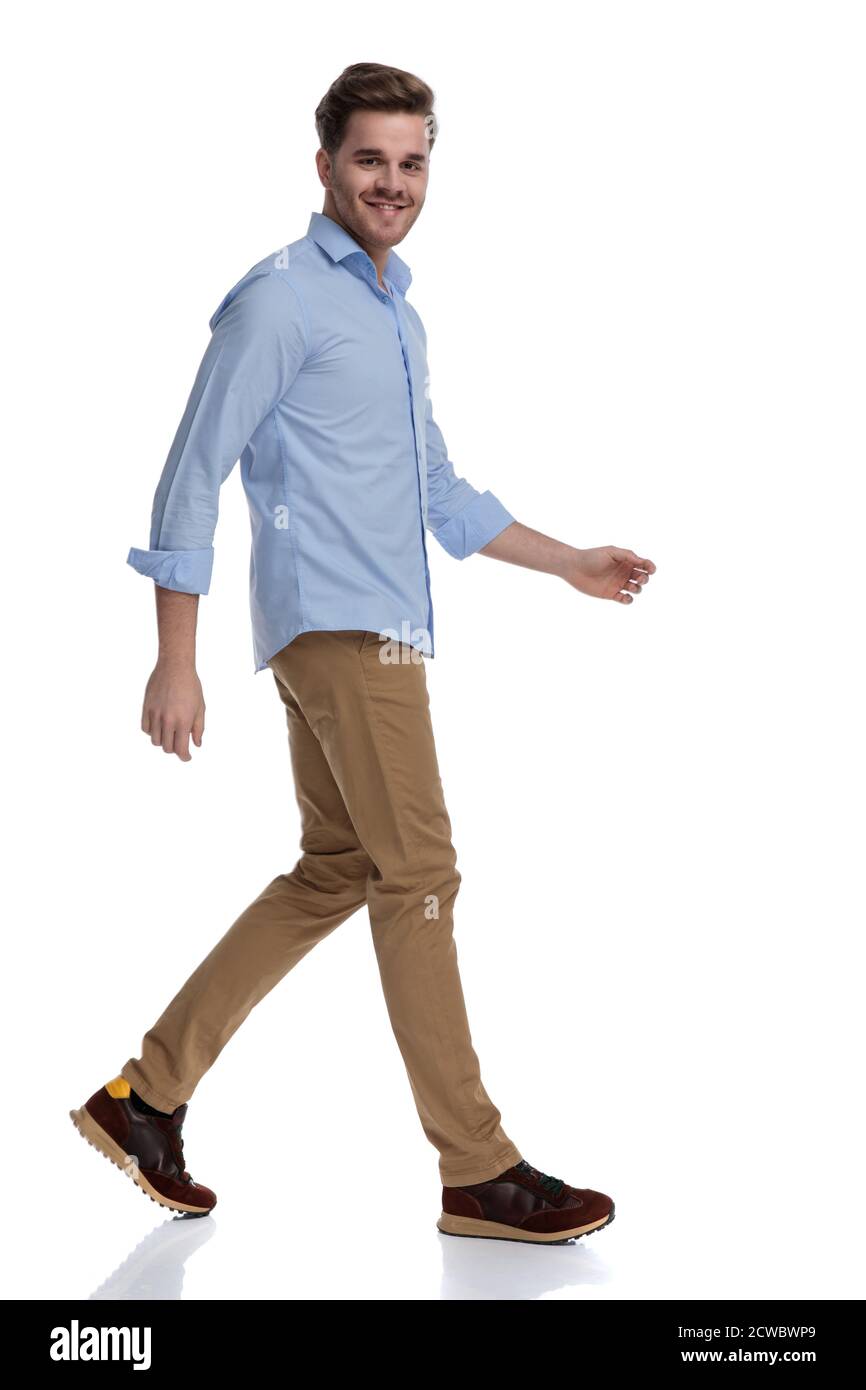 Side view of positive casual man laughing while walking on white studio ...