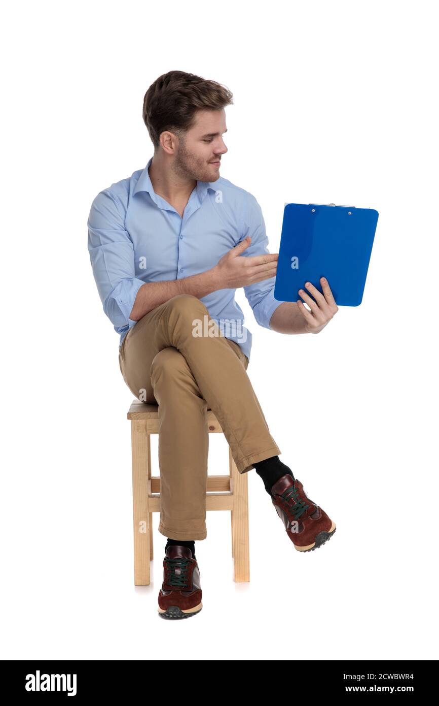 Young casual man presenting clipboard while sitting on a chair on white ...