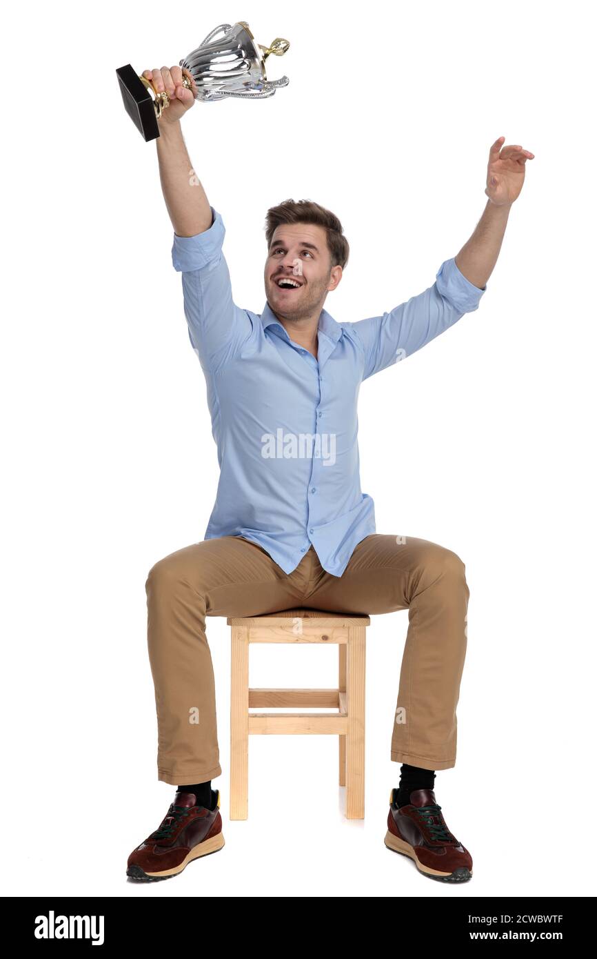 Cheerful casual man holding trophy and celebrating while sitting on a ...