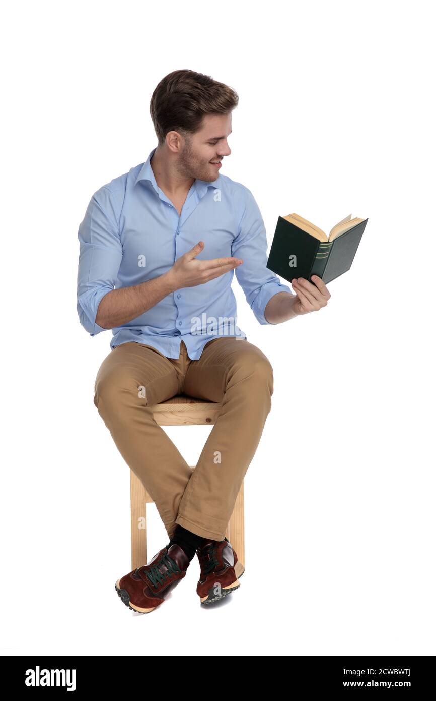Handsome casual man presenting book while sitting on a chair on white ...