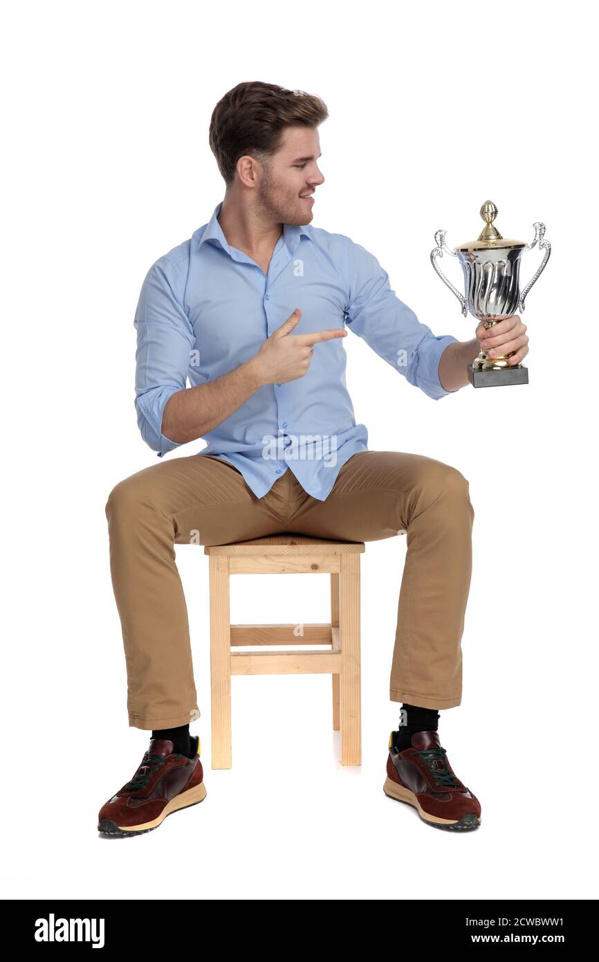 Proud casual man holding trophy and pointing at it while sitting on a ...