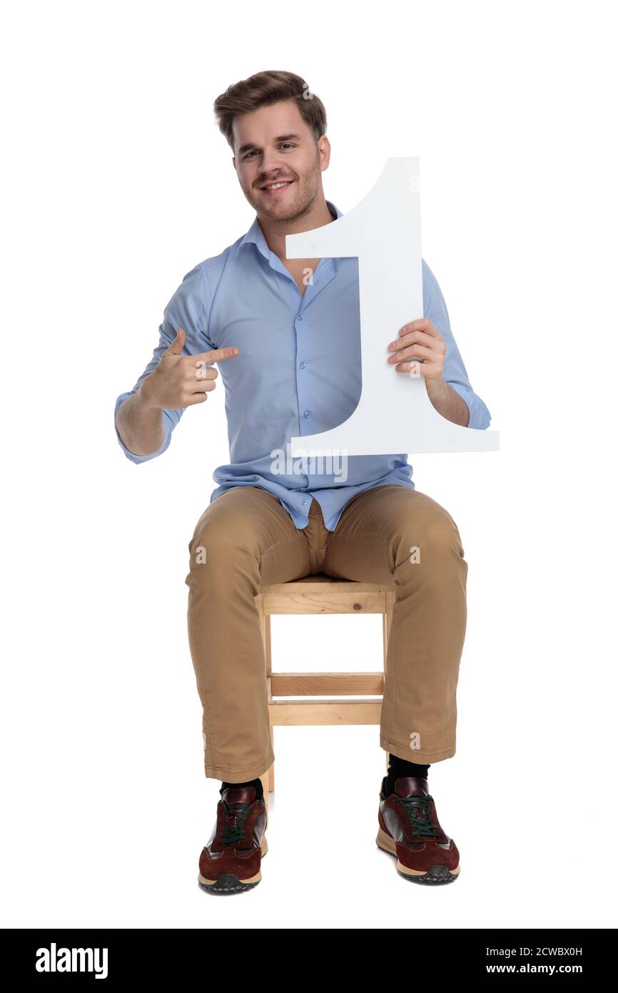 Happy casual man holding number one and pointing to it while sitting on ...