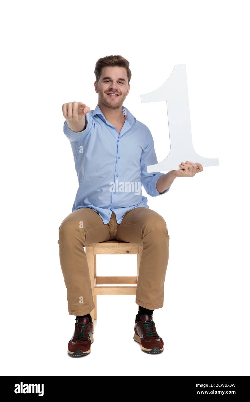 Happy casual man holding number one and pointing while smiling and ...