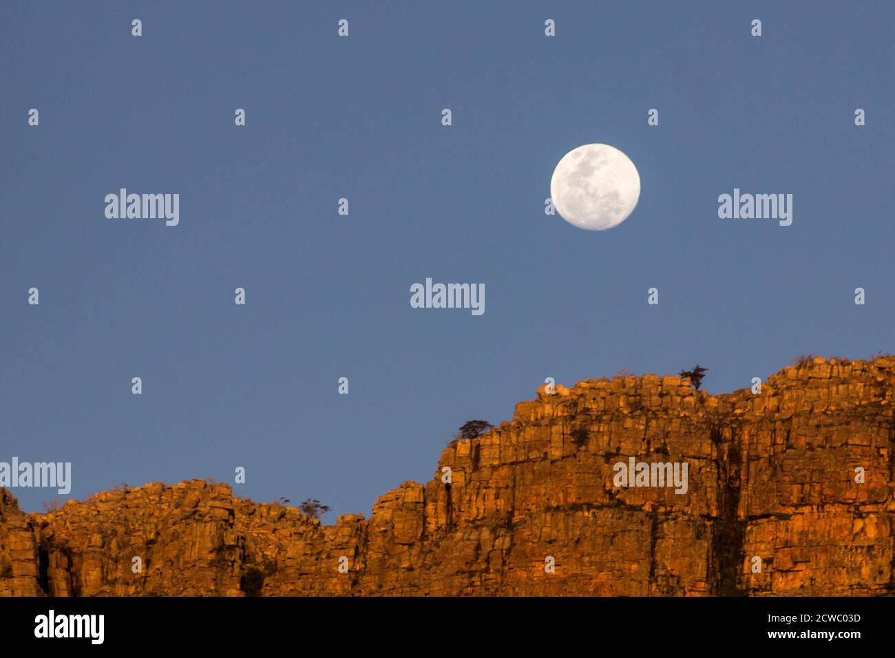 The full moon rising over a reddish colored, sandstone cliff of the ...