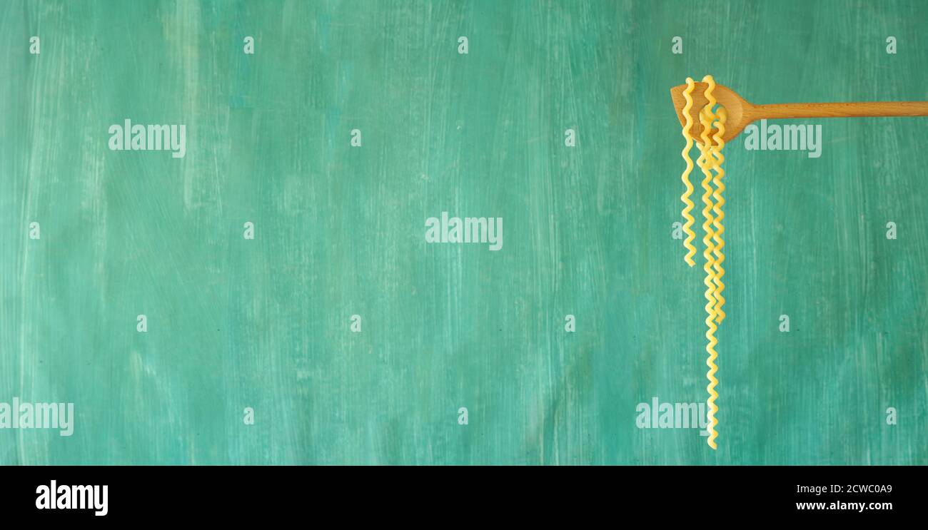 italian fusili spaghetti pasta hanging on a wooden spoon on green ...